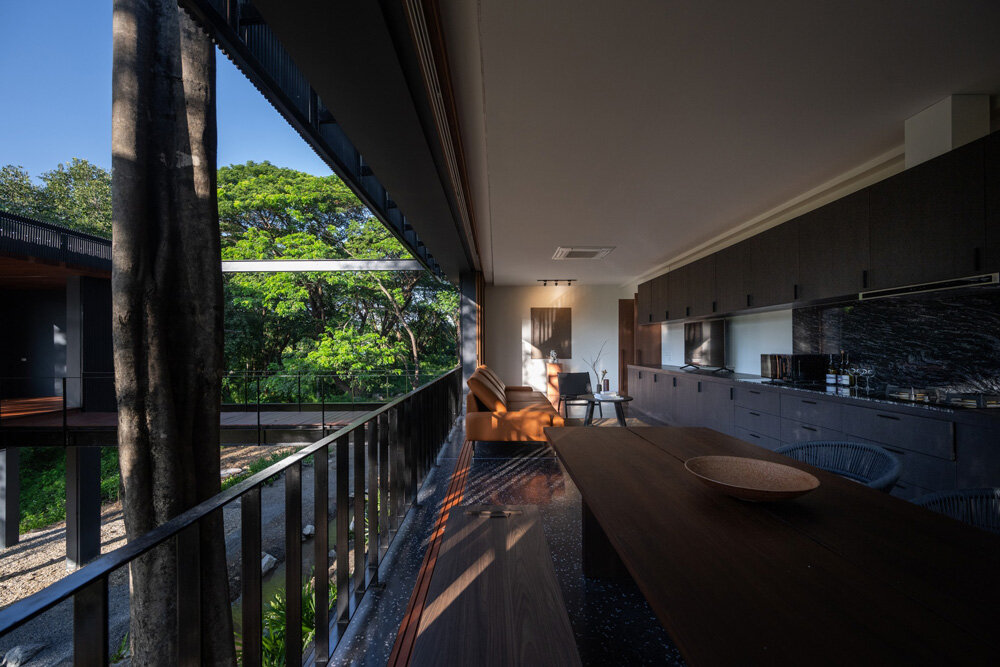 timber-clad residence settles on stilts within raintree forest in thailand