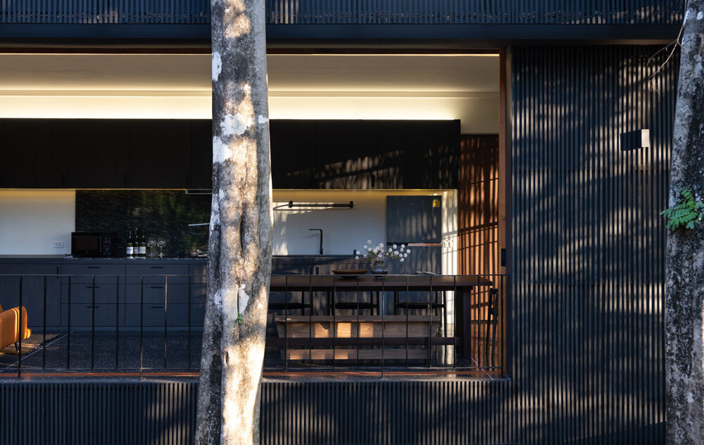 timber-clad residence settles on stilts within raintree forest in thailand