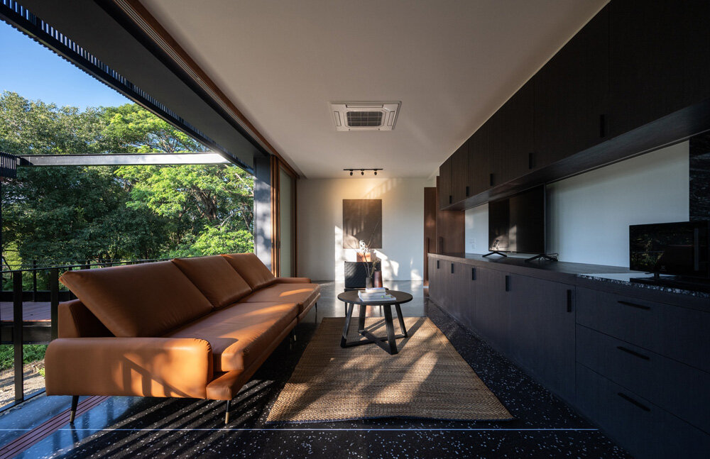 timber-clad residence settles on stilts within raintree forest in thailand